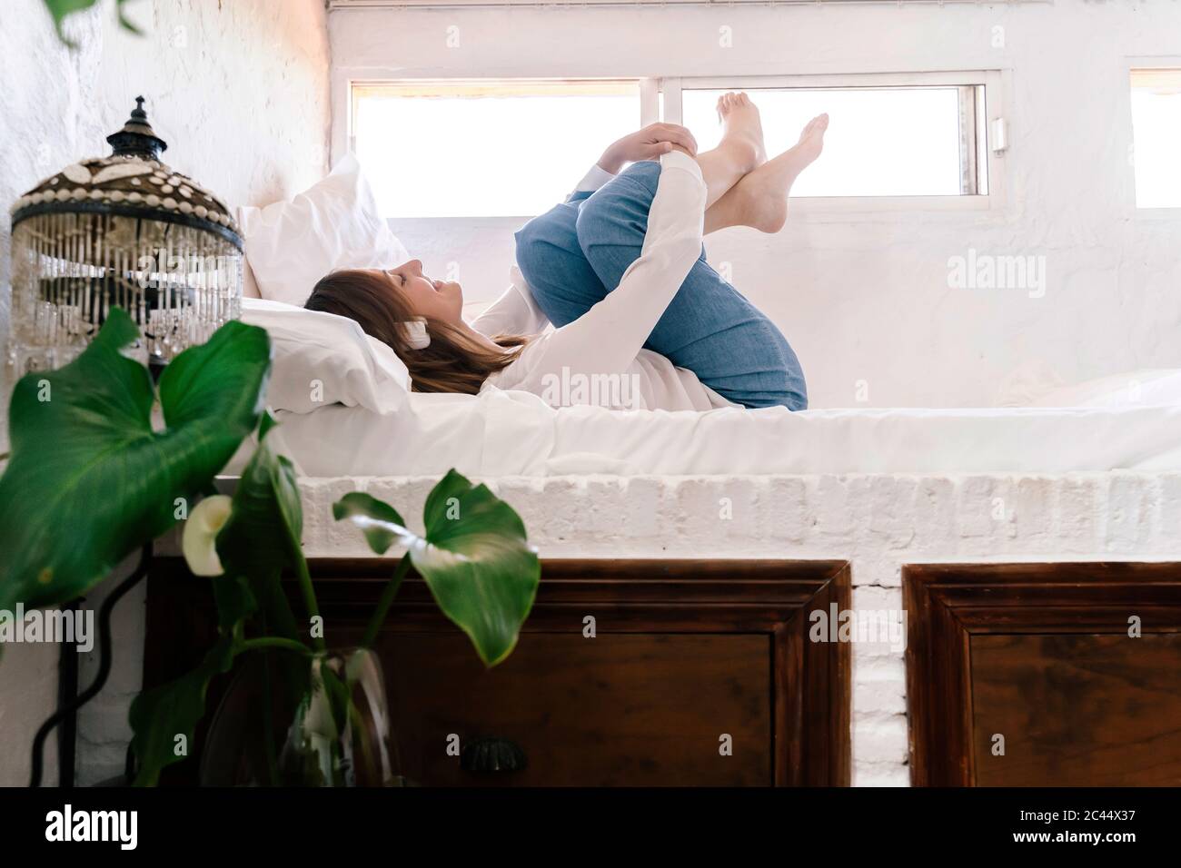 Happy woman lying on bed listening music with headphones Stock Photo ...