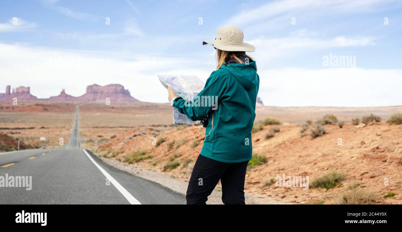 Female tourist reading map while standing on roadside against sky ...
