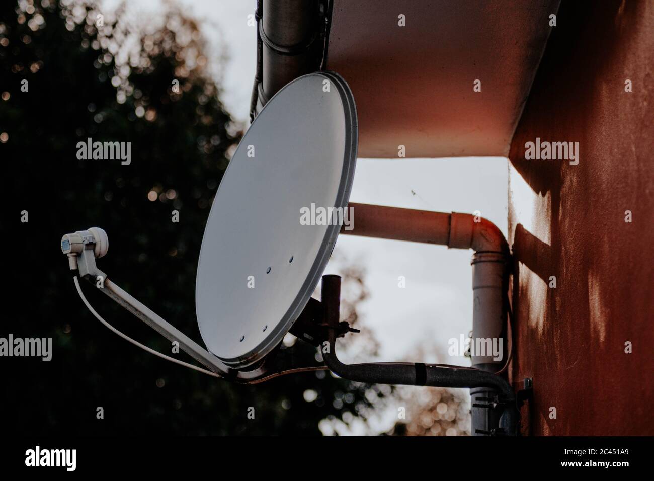 Closeup shot of a white satellite dish on fixed on a red wall with ...