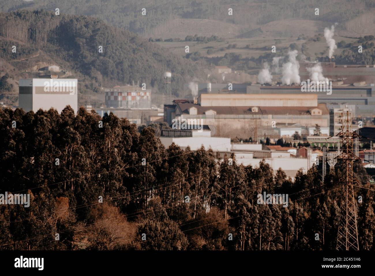 Aerial shot of industrial factories surrounded by hills with trees on ...