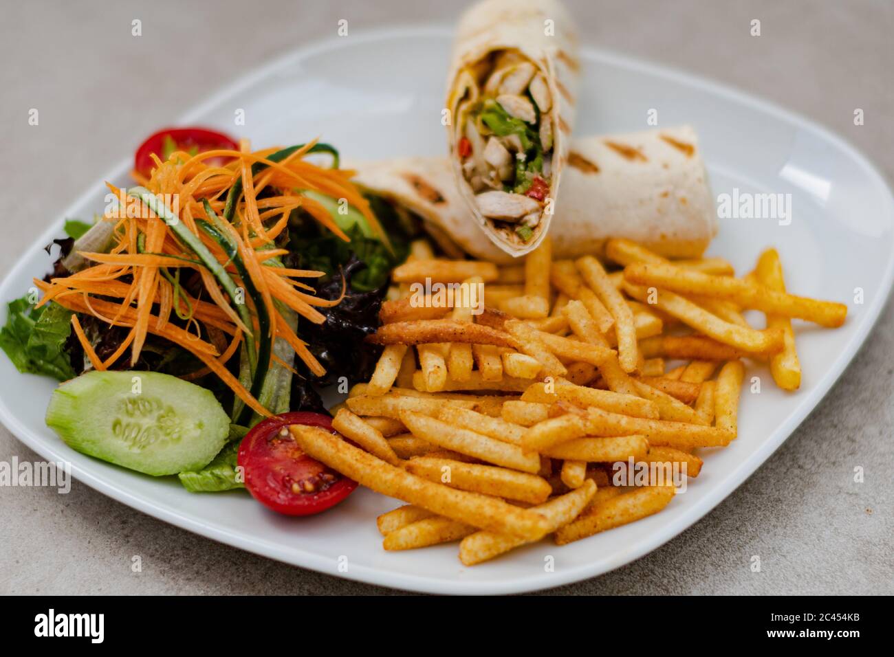 Wrap served with fried potatoes and vegetable salad Stock Photo - Alamy