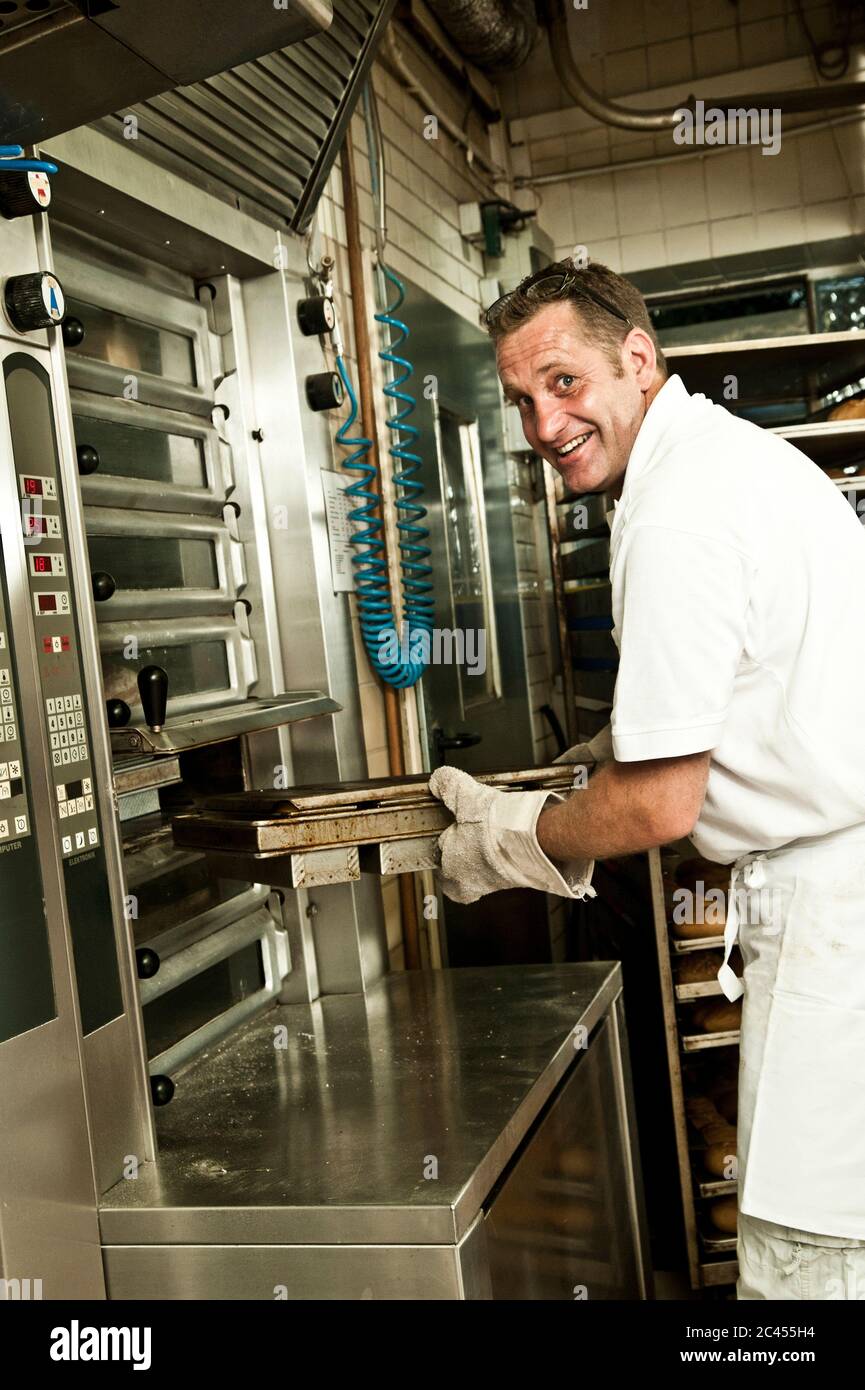 Smiling baker at the oven in a bakery Stock Photo - Alamy