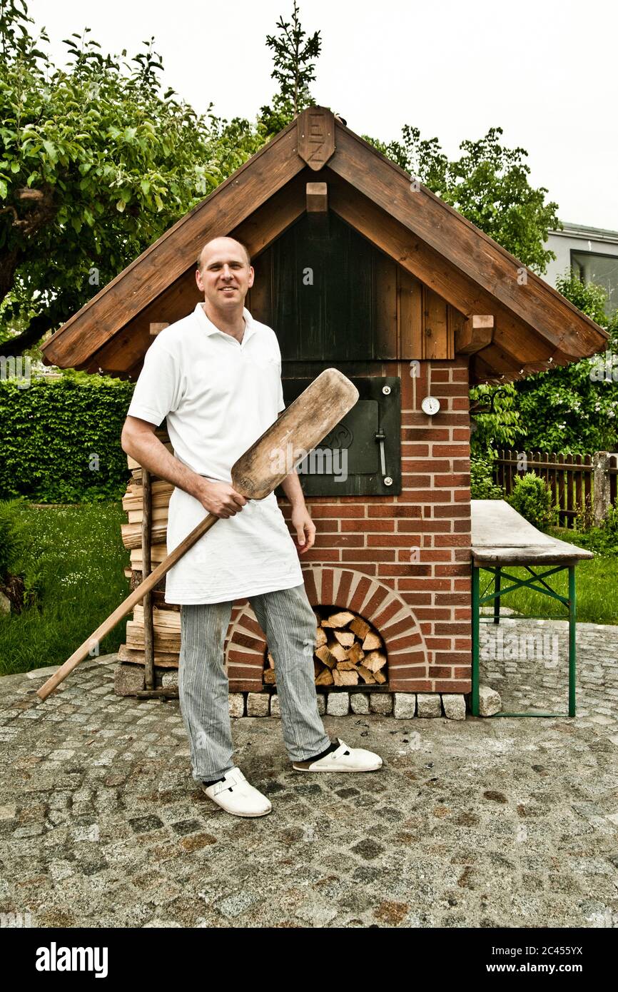 A smiling baker is standing by the outside oven of a bakery Stock Photo ...