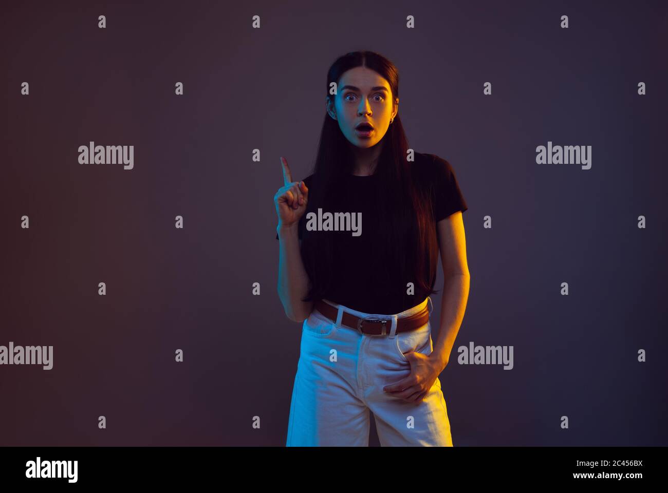 Shocked pointing up. Caucasian young woman's portrait on dark studio ...
