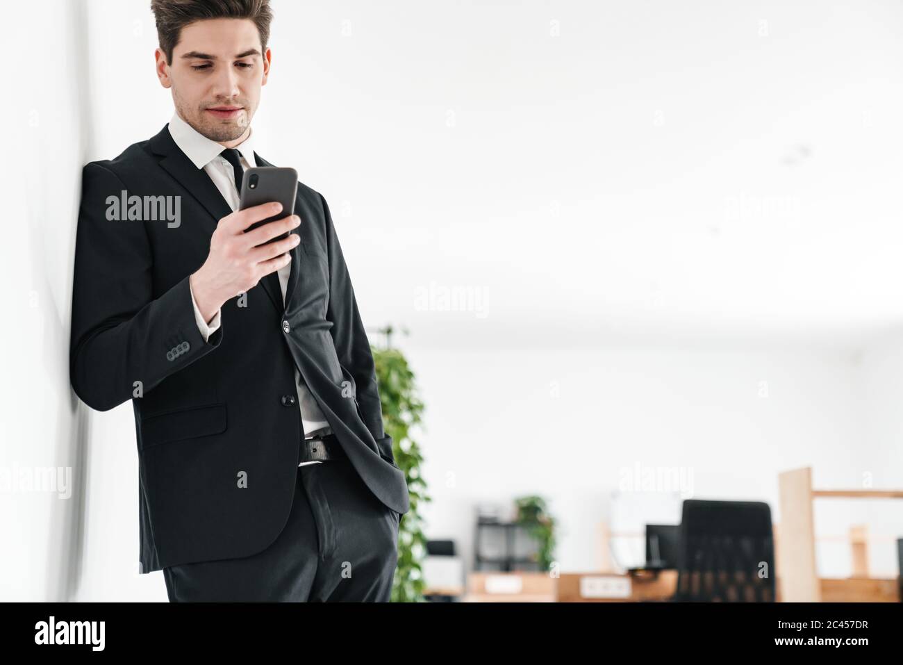 Image of serious young businessman wearing black suit using mobile ...