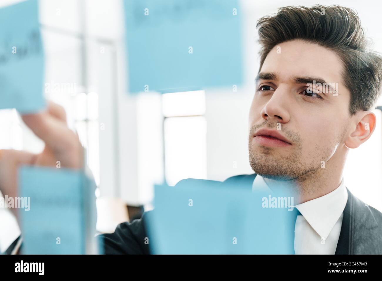 Image of concentrated young businessman wearing suit using stickers ...