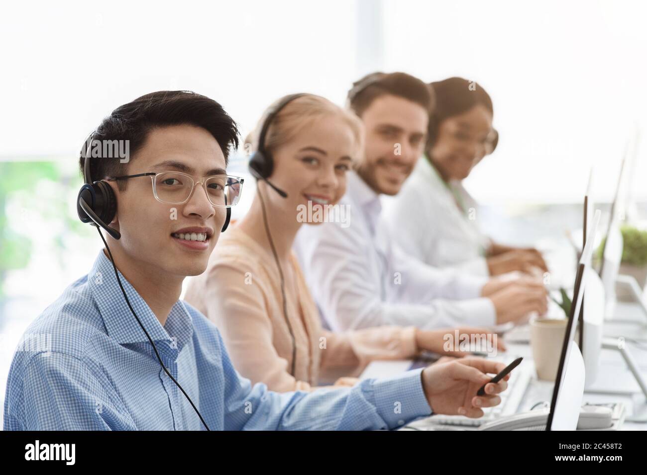 Smiling call center workers sitting in row near their computers at ...