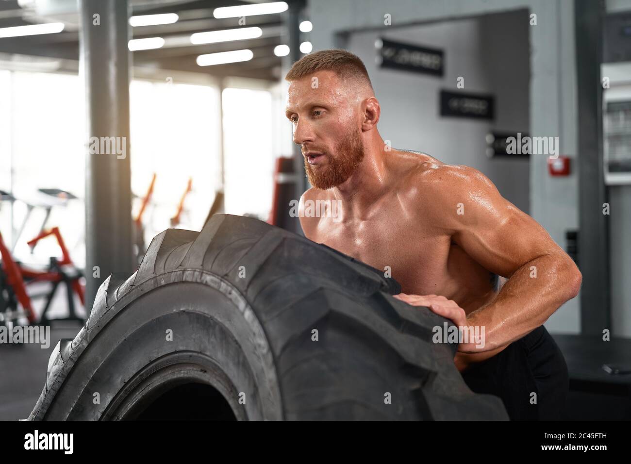 Athlete sportive man lift wheel gym cross training push big tire Middle ...