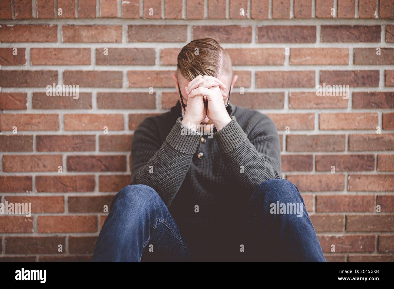 Young male sitting on the ground and holding his hands together Stock ...