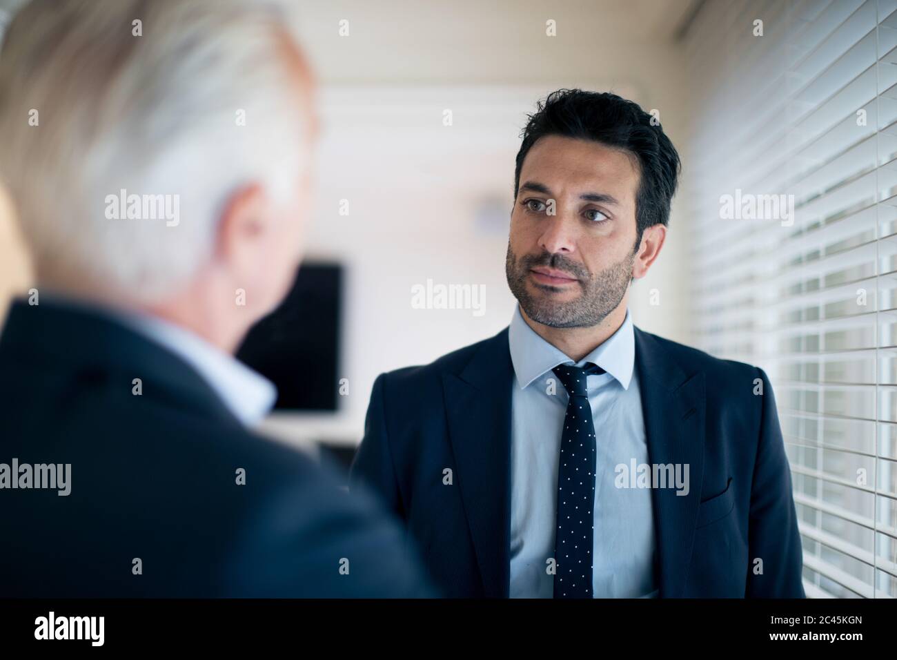 Two businessmen standing indoors, talking Stock Photo - Alamy