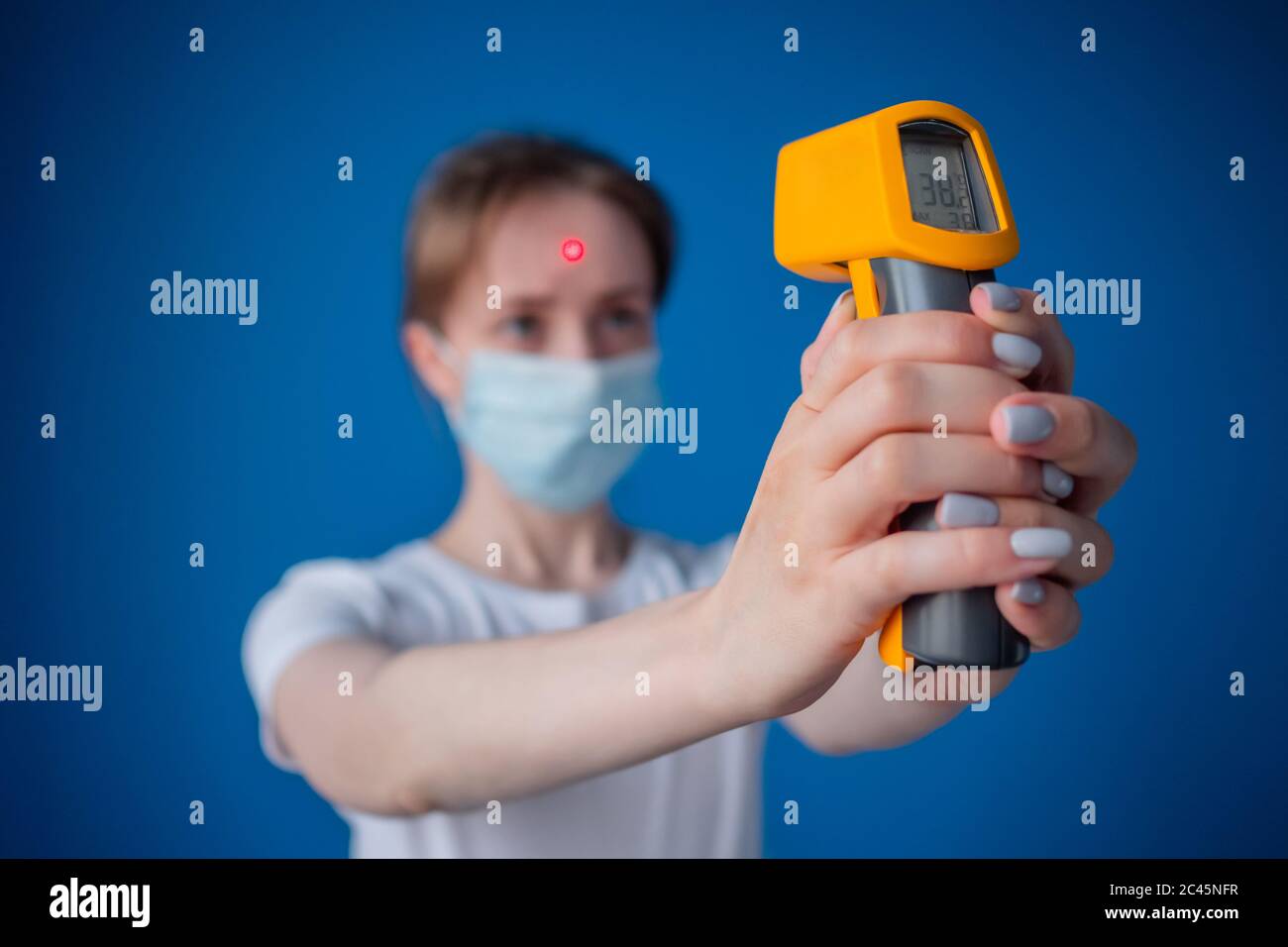 Woman in medical face mask holding yellow pyrometer to measure body ...