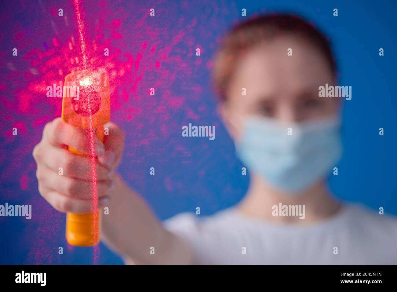 Woman in medical face mask holding yellow pyrometer to measure ...