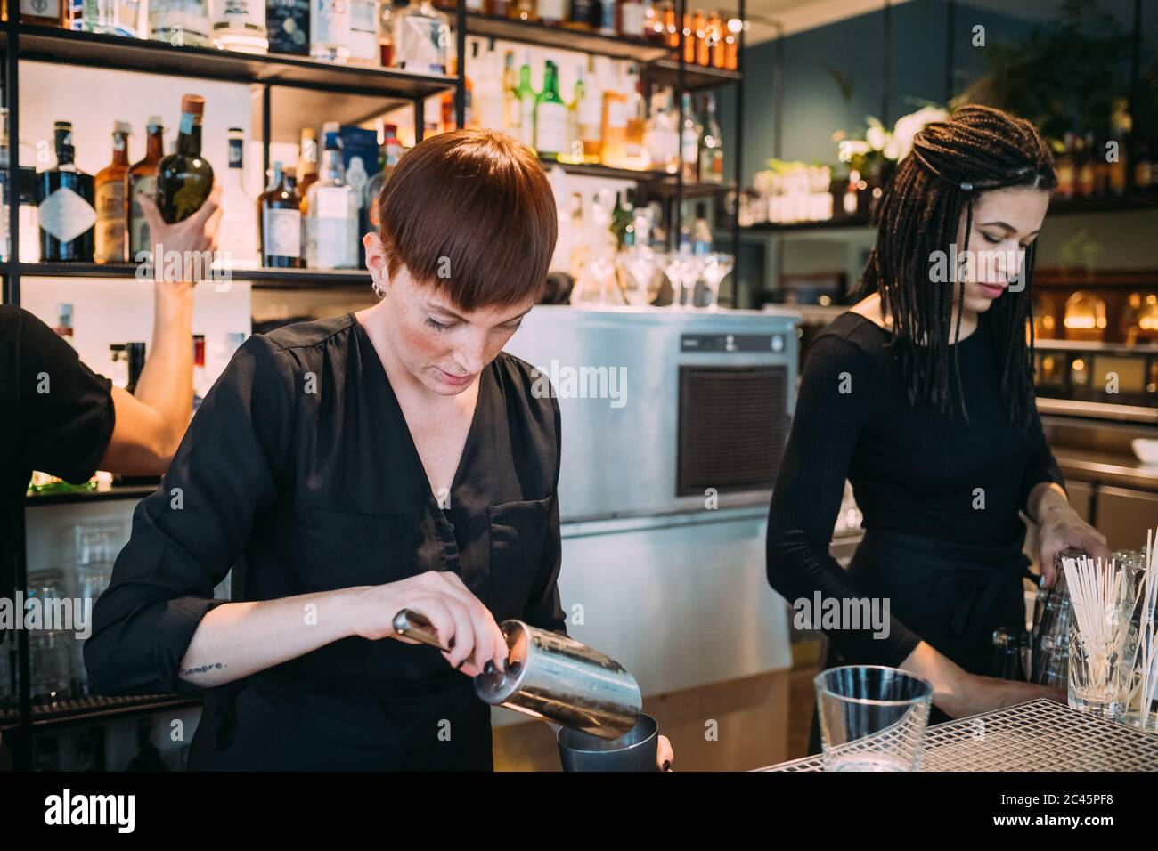 Two young women wearing black clothes standing behind bar counter ...