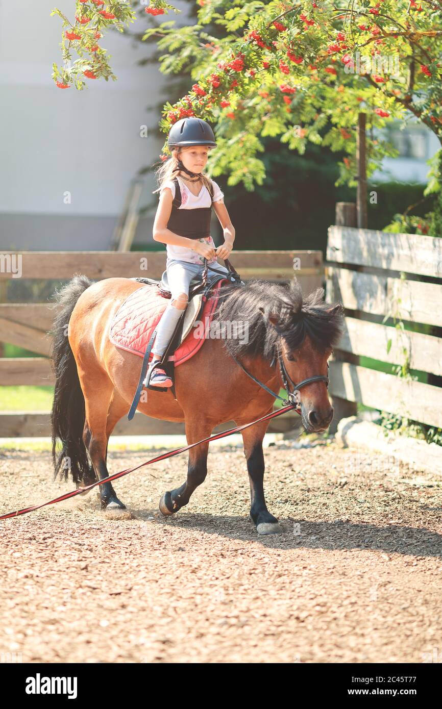 Young Caucasian girl riding on a pony, having longe line riding lesson ...