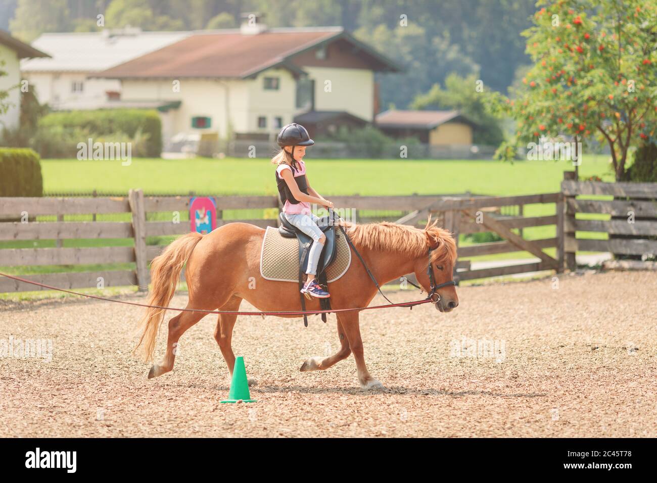 Young Caucasian girl riding on a pony, having longe line riding lesson ...