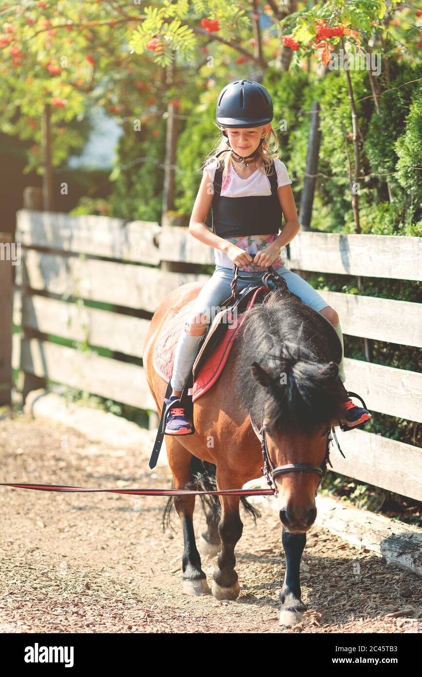 Young Caucasian girl riding on a pony, having longe line riding lesson ...