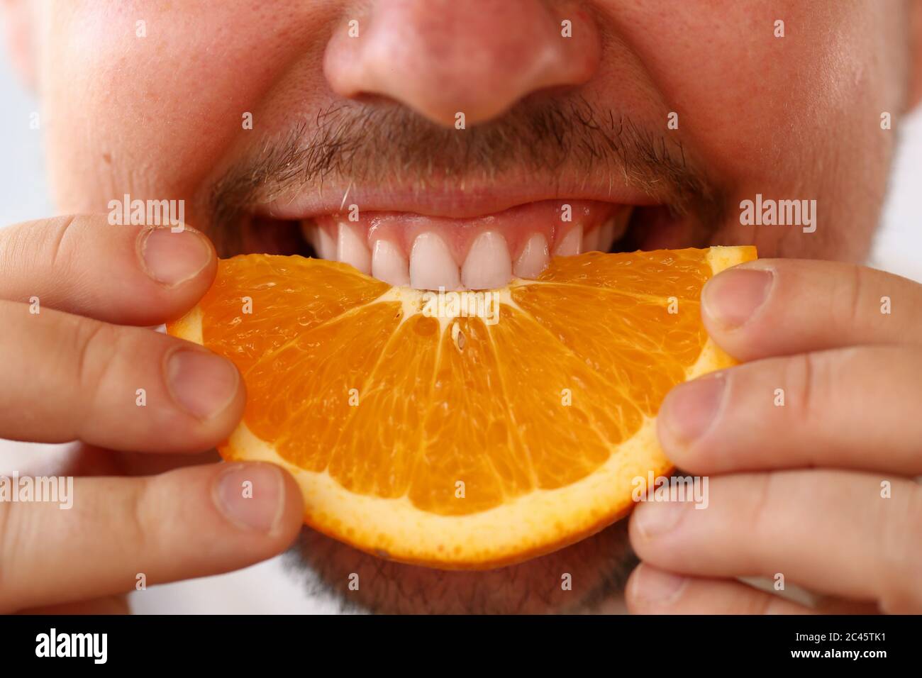 Bearded young man biting juicy orange half Stock Photo - Alamy