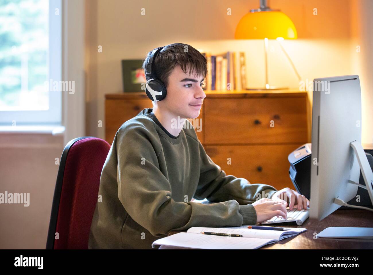 Boy wearing headphones sitting at desk in front of computer, studying ...