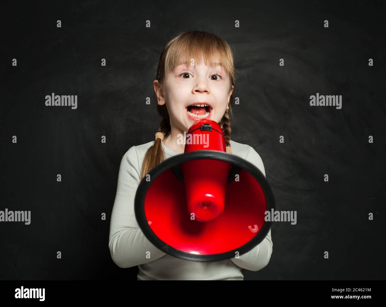 Little girl shouting through a megaphone on black background. Kid with ...