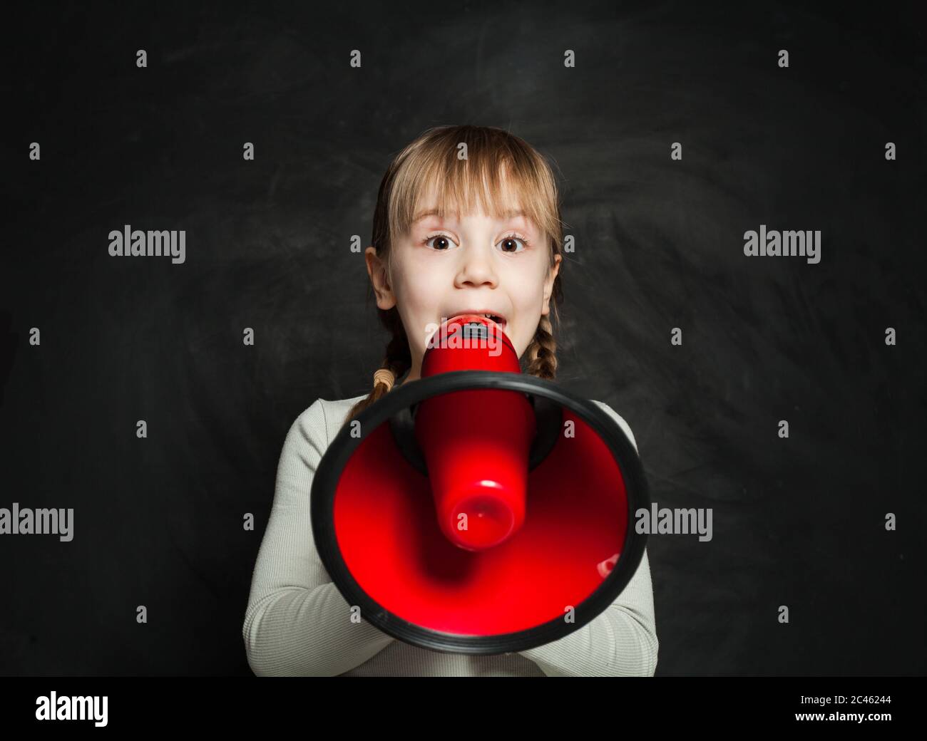 Happy child girl speaking through a megaphone on blackboard background ...