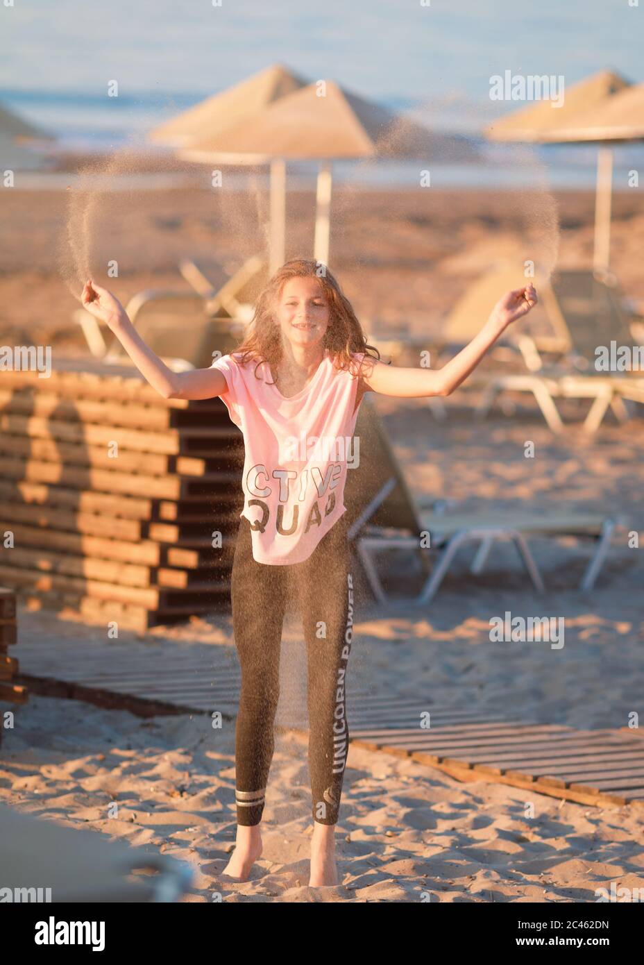 Young Girl Tween Age Wearing Casual Summer Clothing Throwing Sand In The Air On The Beach