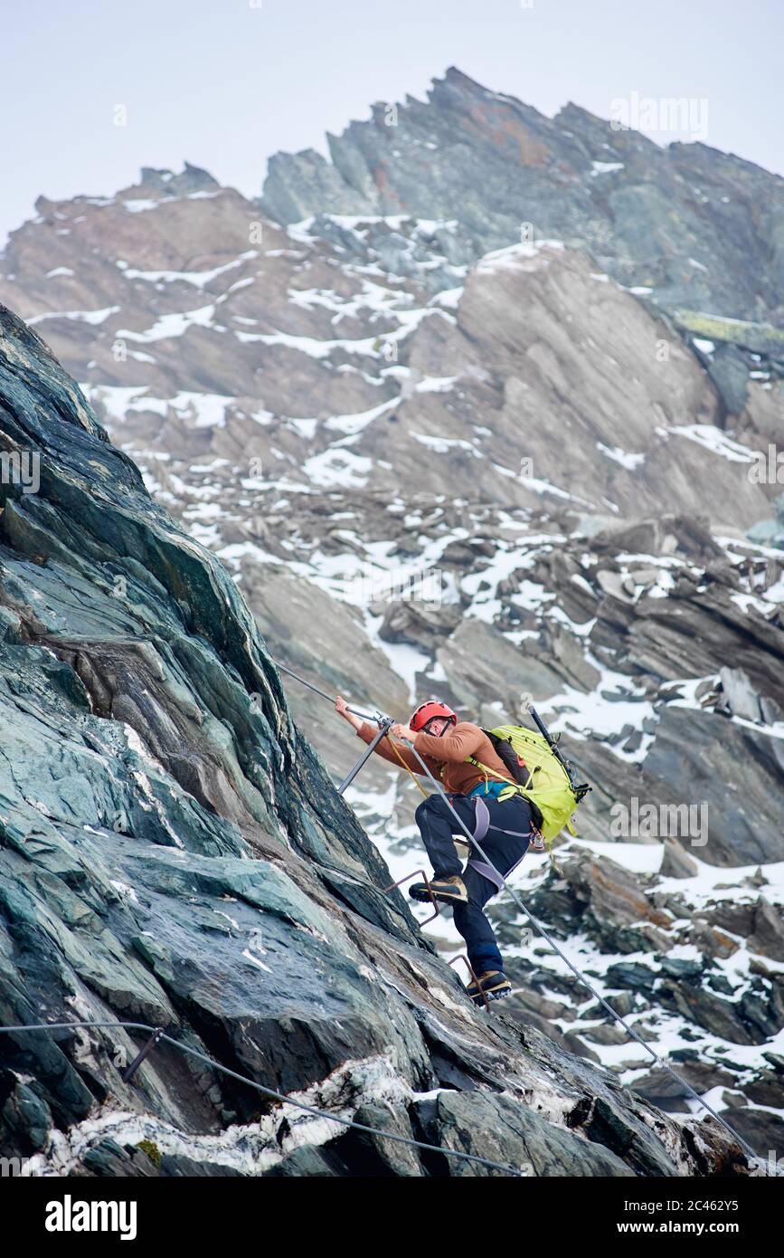 Side view alpinist with backpack using fixed rope to climb high rocky ...