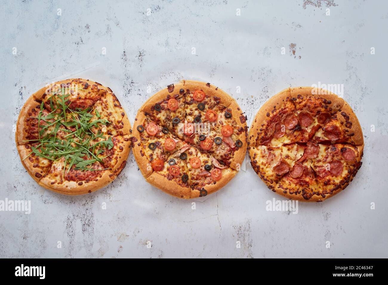 Three different kind of pizzas placed in a row on white rusty table ...