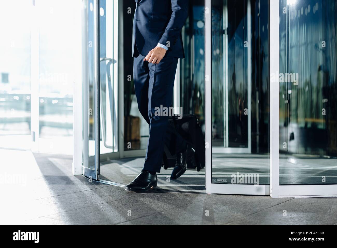 Businessman with wheeled luggage exiting revolving doors of building ...