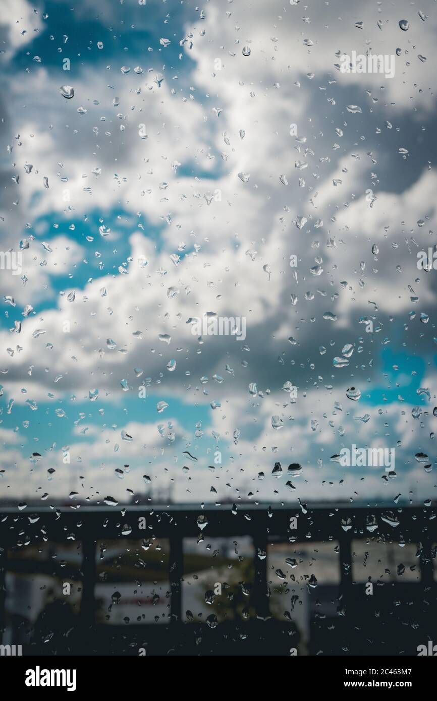 Glass with raindrops and blurred fluffy clouds from the other side of ...