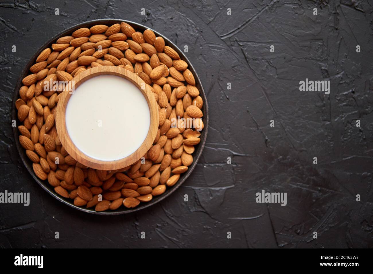 Composition of almonds seeds and milk, placed on black stone background ...