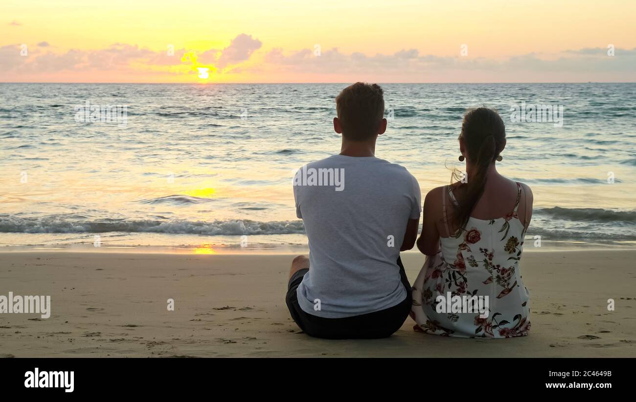lovely young couple sits on empty ocean beach watching sunset at ...