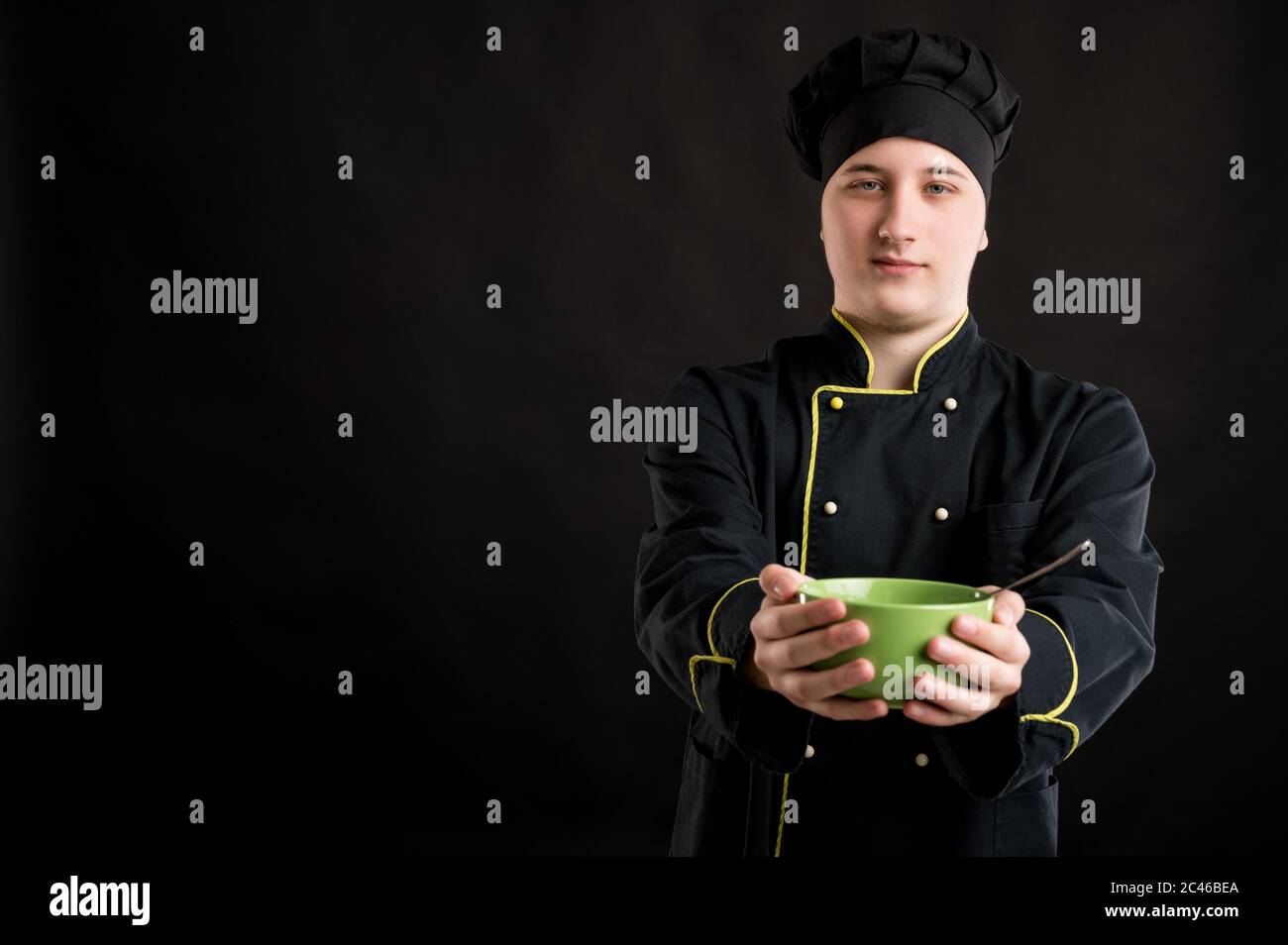 Portrait of young male dressed in a black chef suit give the bowl of ...