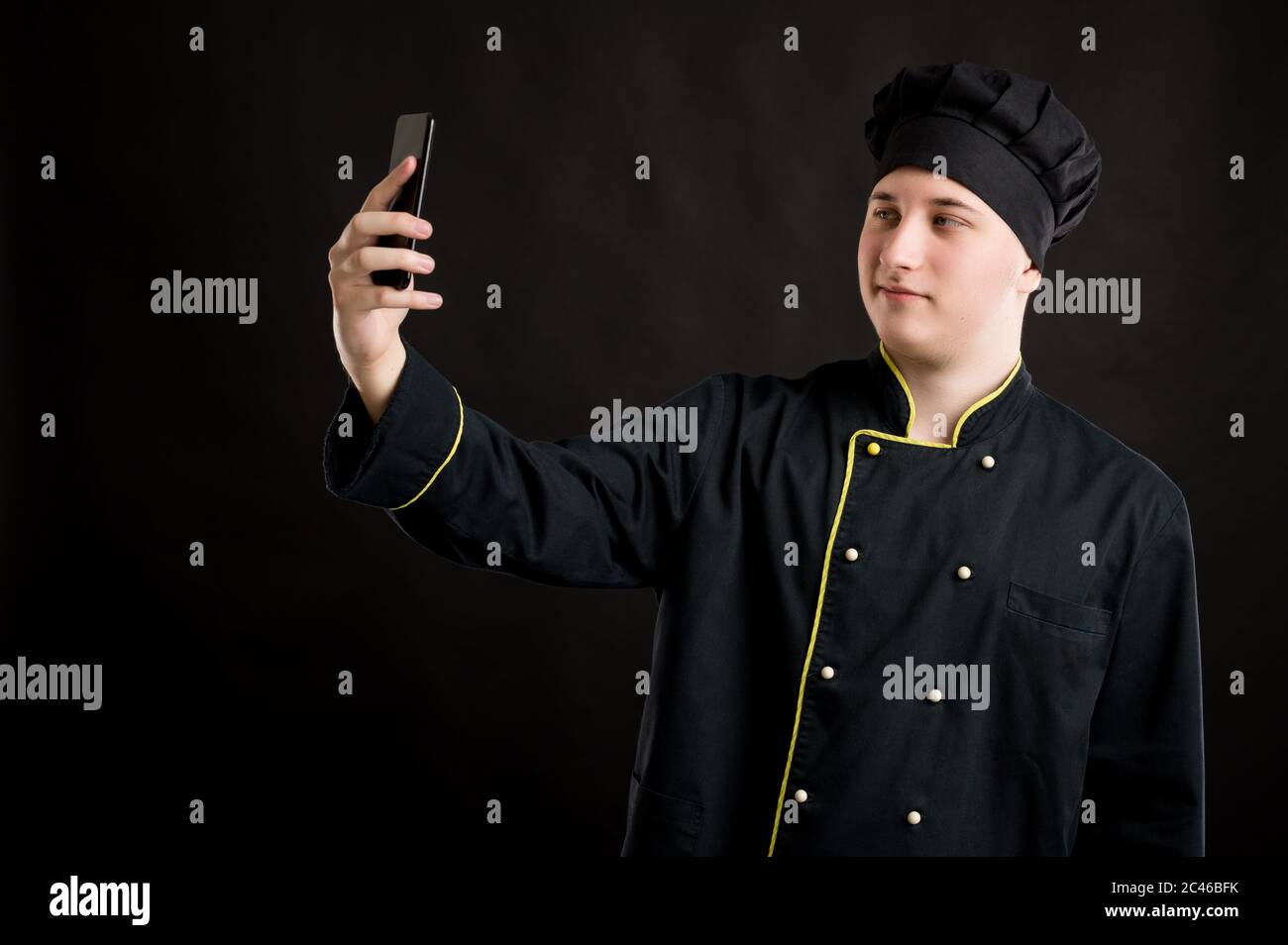 Portrait of young male dressed in a black chef suit taking selfie ...