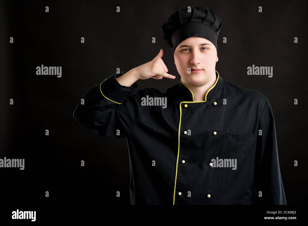 Portrait of young male dressed in a black chef suit showing call me ...