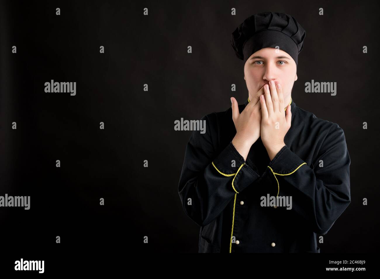Portrait of young male dressed in a black chef suit covering mouth like ...