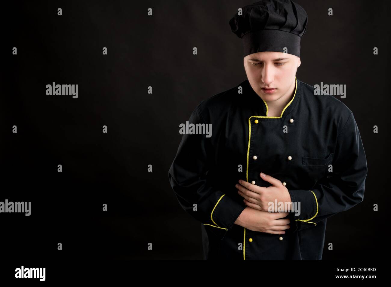 Portrait of young male dressed in a black chef suit has stomach pain ...
