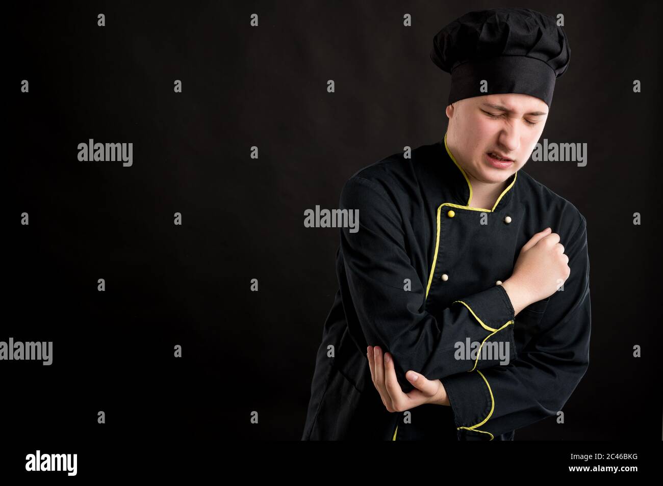 Portrait of young male dressed in a black chef suit elbow pain posing ...