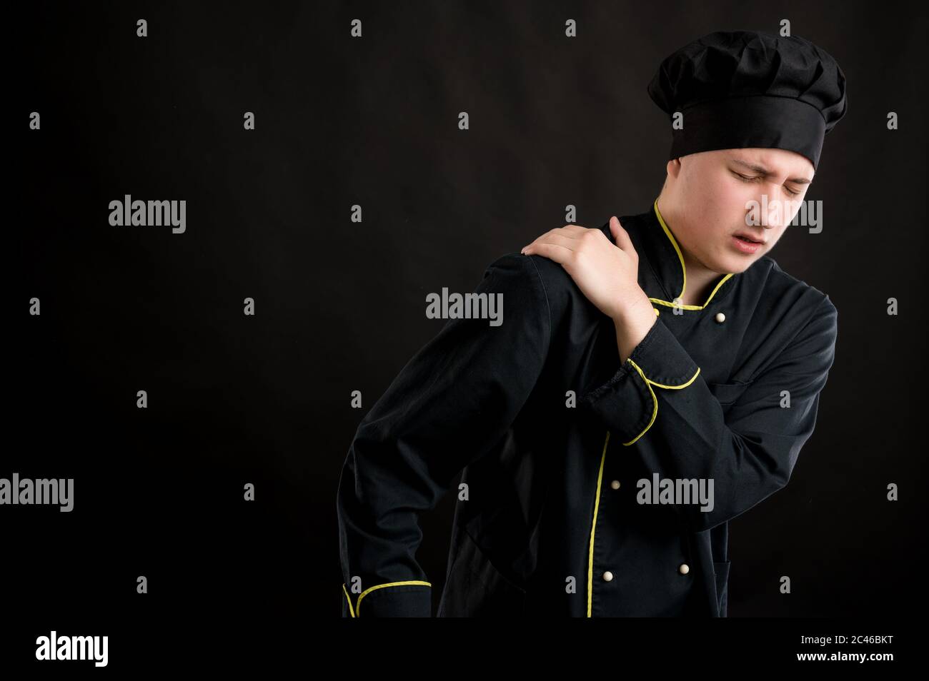 Portrait of young male dressed in a black chef suit has shoulder pain ...
