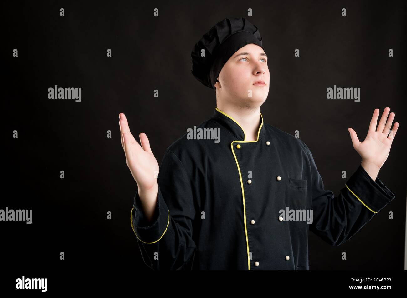 Portrait of young male dressed in a black chef suit with open arms ...