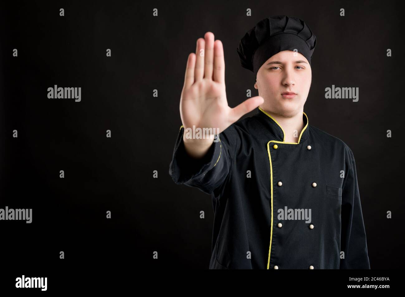 Portrait of young male dressed in a black chef suit showing stop sign ...