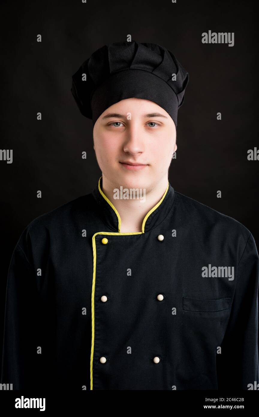 Portrait of young dressed in a black chef suit posing on a black ...