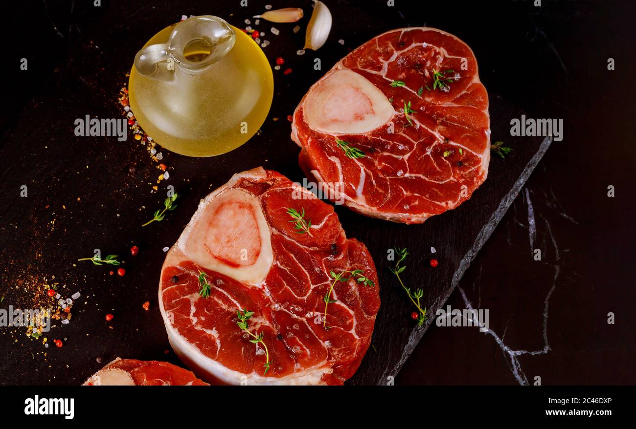 Fresh uncooked cut beef shank in bone and seasonings in spoons on black ...