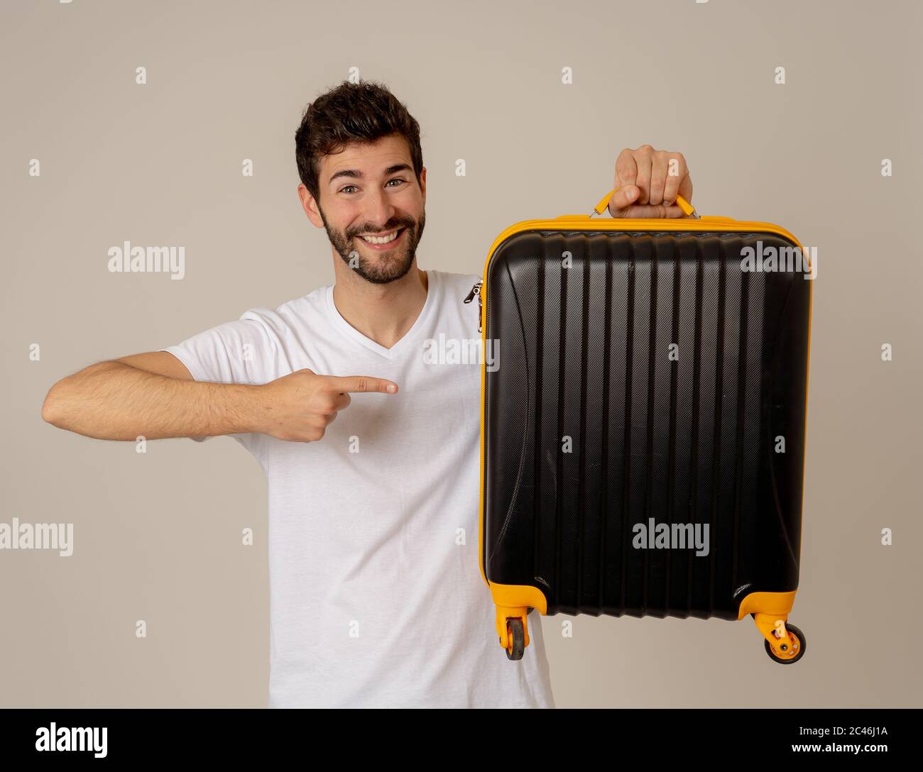 Attractive young traveler man showing suitcase isolated on neutral ...