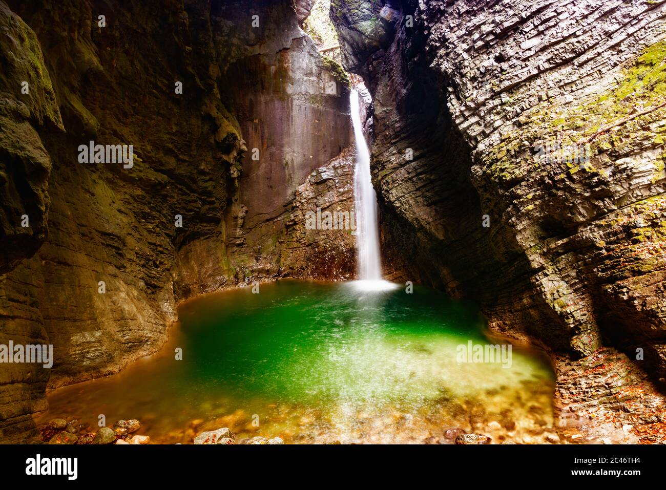 the waterfall flows from the mountain and falls into a green lake on a ...