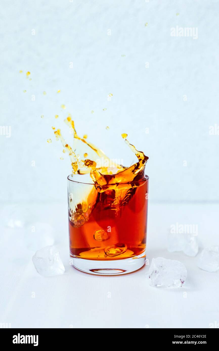 A photo of a cocktail splash, rocks glass, ice cubes around, light blue ...