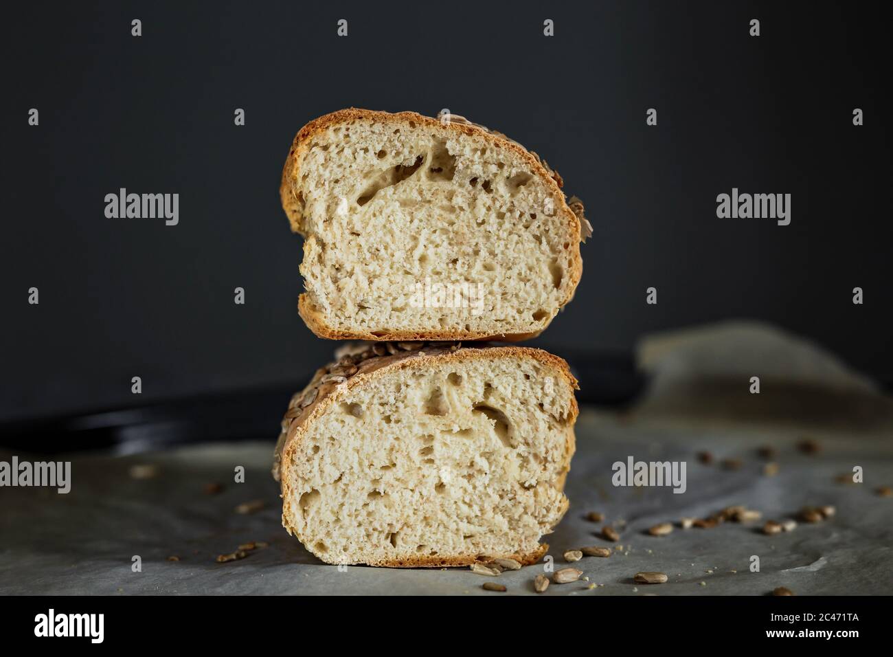 A homemade bread cut in half, covered in sunflower seeds, on baking ...