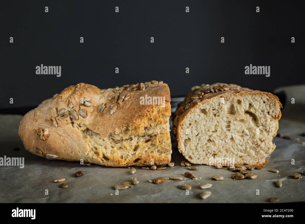 A homemade bread cut in half, covered in sunflower seeds, on baking ...