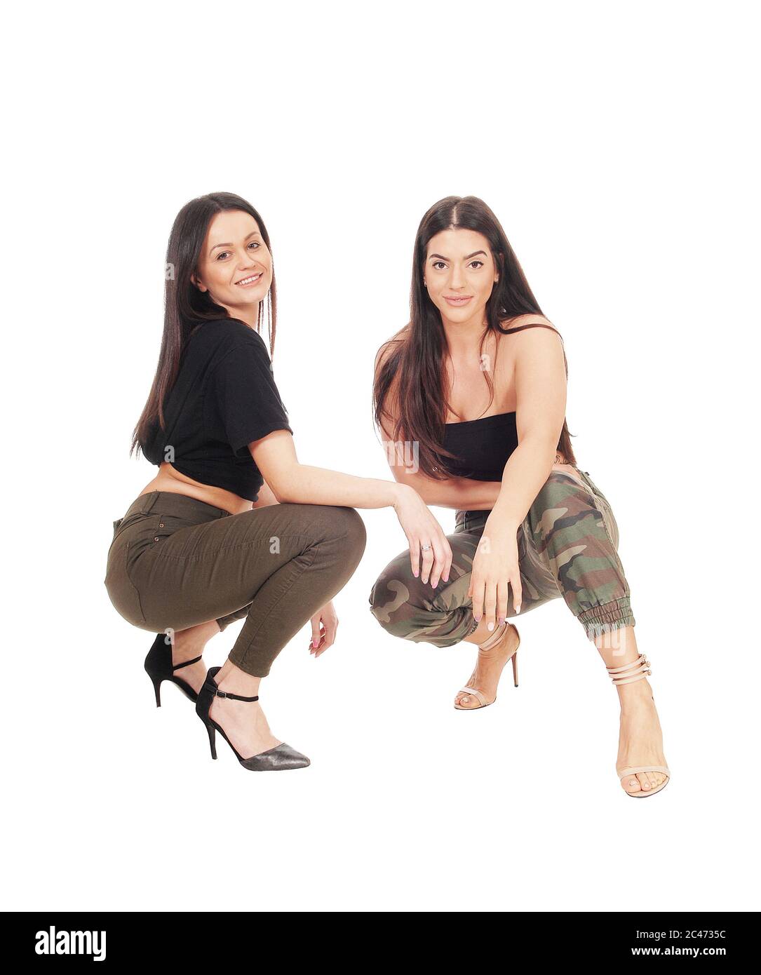 Two beautiful young woman crouching side by side in jeans and heels ...