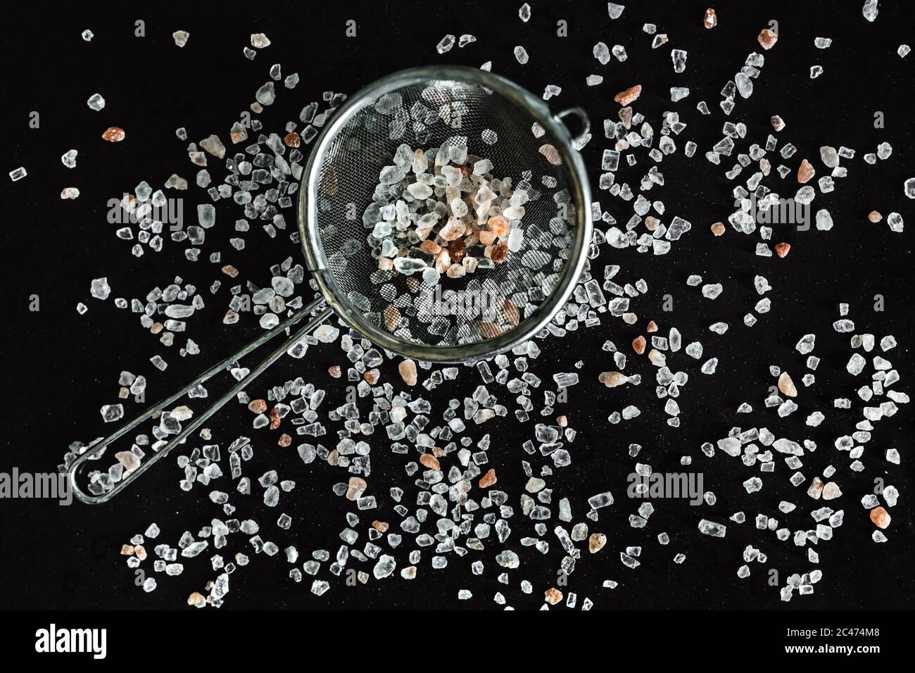 Himalayan pink salt and a strainer on black background, top view photo ...