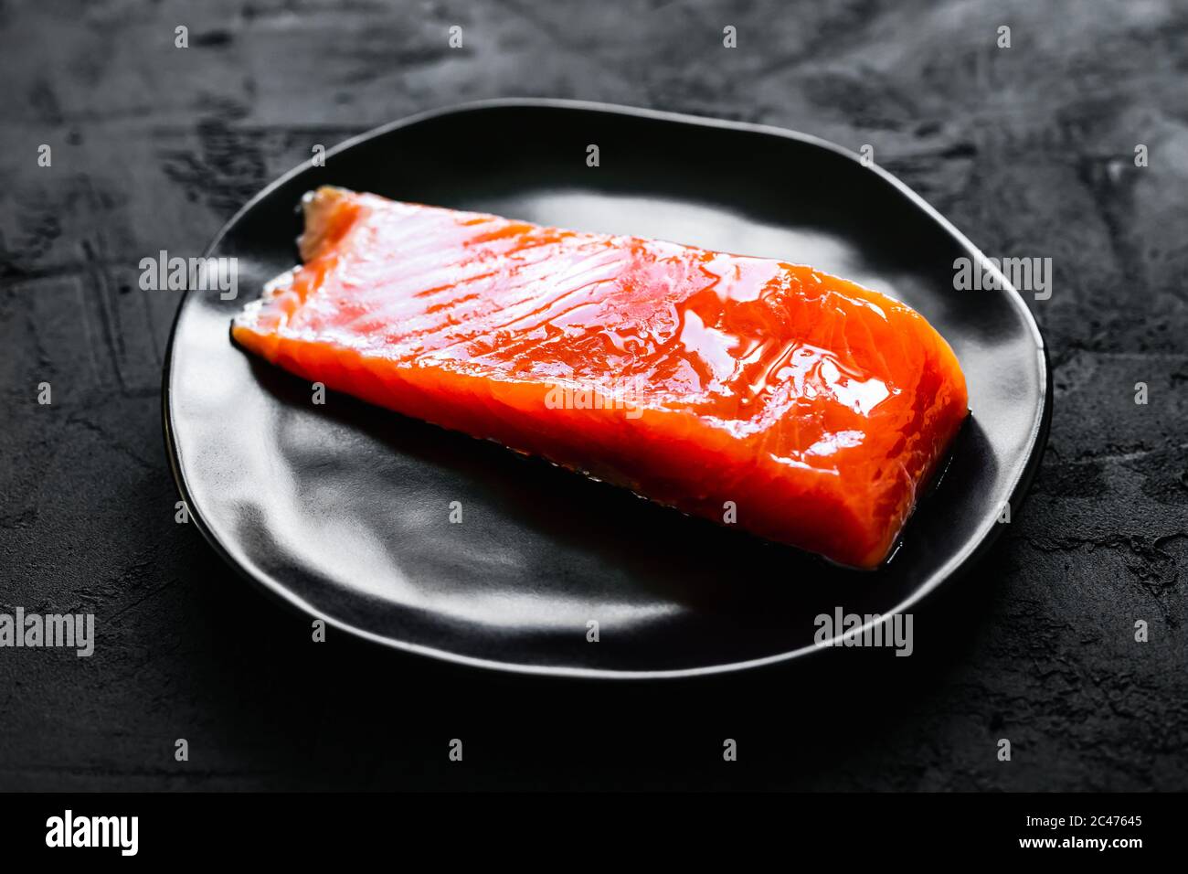Salted red fish on a black plate on black background, a close-up photo ...